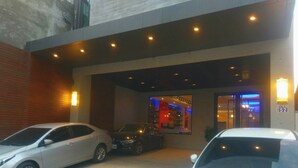 Uma área de estacionamento com dois carros estacionados em frente a um edifício de design moderno, com uma grande janela e uma placa com caracteres japoneses.