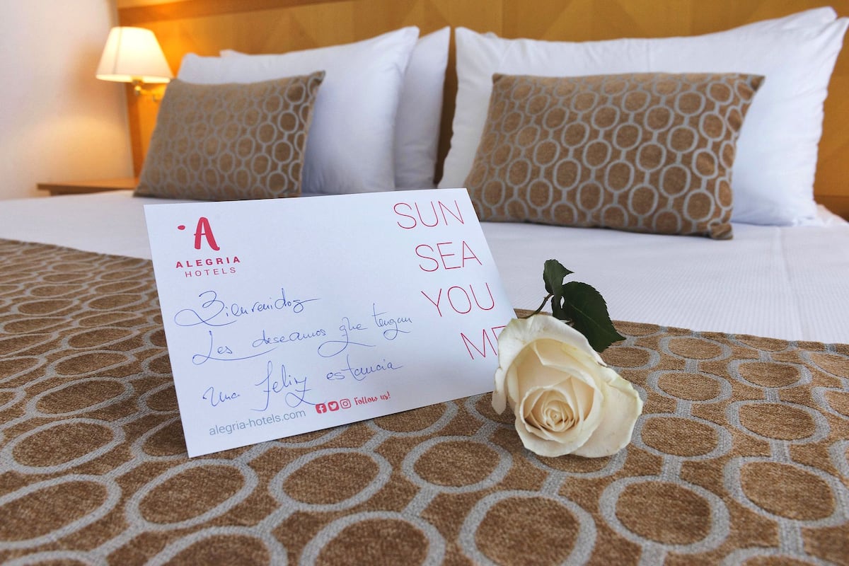 Uma cama de hotel com um bilhete e uma rosa. O bilhete diz 'Sol Mar Você Eu' e 'Zilverenweg'.