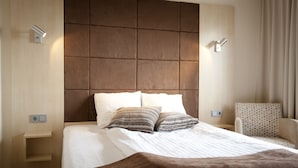 Quarto de hotel moderno com uma cama grande, cabeceira acolchoada, mesa de apoio e poltrona estampada.
