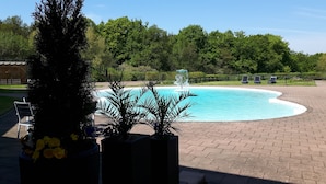 Uma piscina com uma fonte, cercada por um pátio de tijolos e vegetação.