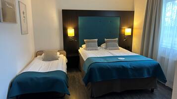 Quarto de hotel com duas camas de solteiro, cabeceira escura, luminárias laterais e janela com cortinas.