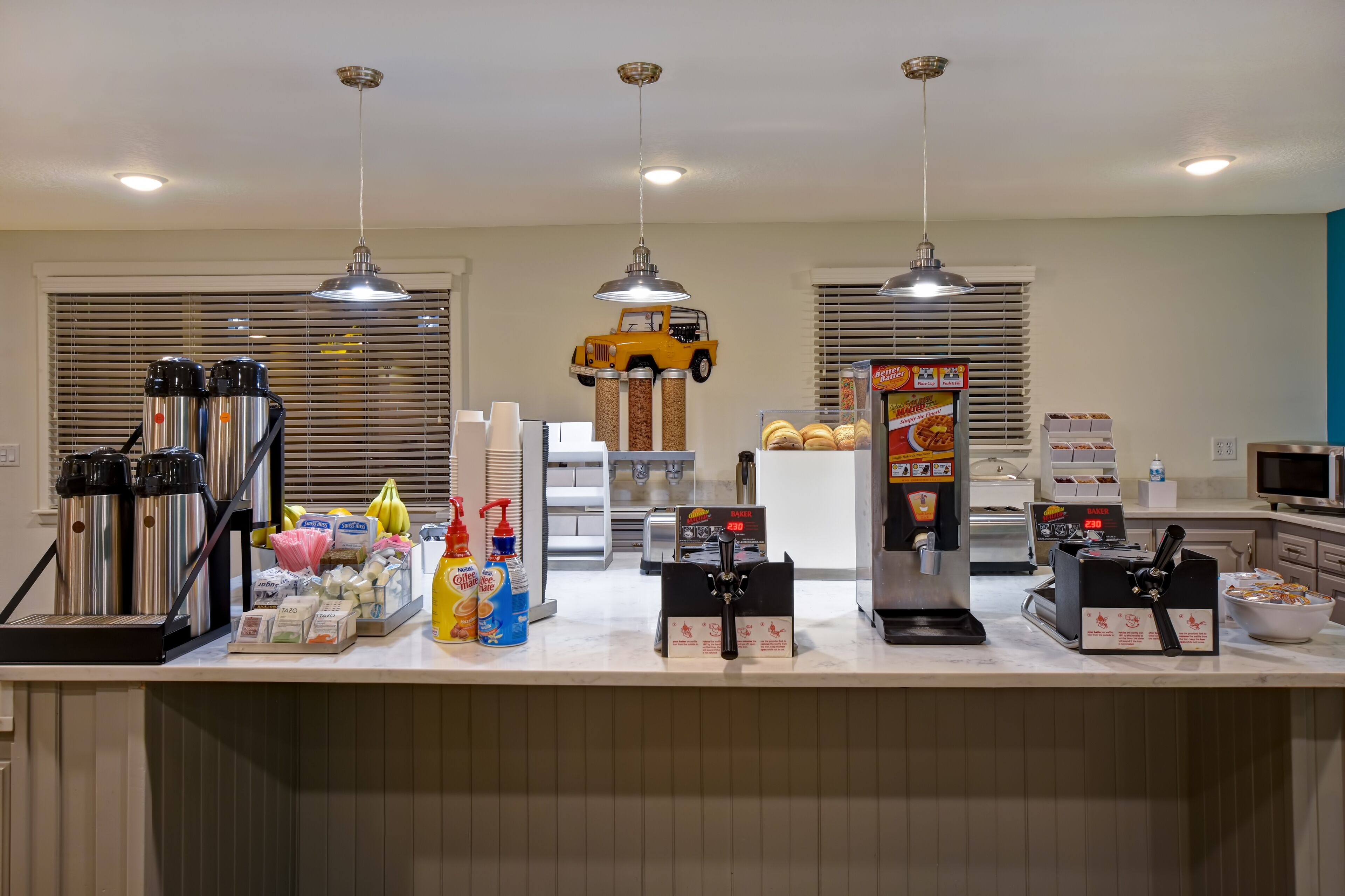 Um balcão de café da manhã com máquinas de café, um carrinho de brinquedo e diversos alimentos.