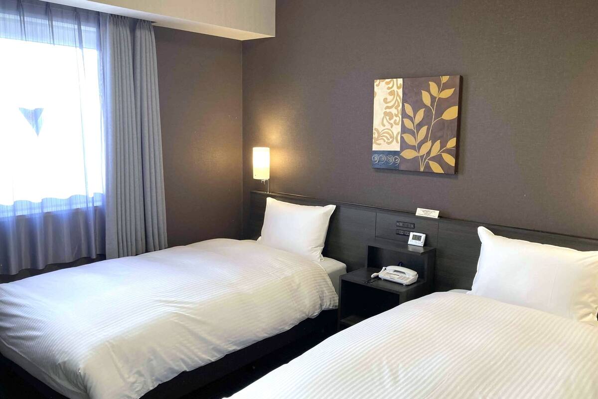 Quarto de hotel com duas camas, mesa de cabeceira com telefone e luminária na parede.
