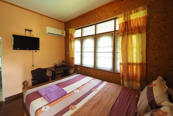 Quarto com cama, escrivaninha, cadeira, televisão e janela com cortinas.