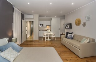 Uma sala de estar moderna com um sofá, uma mesa de jantar e uma cozinha ao fundo.