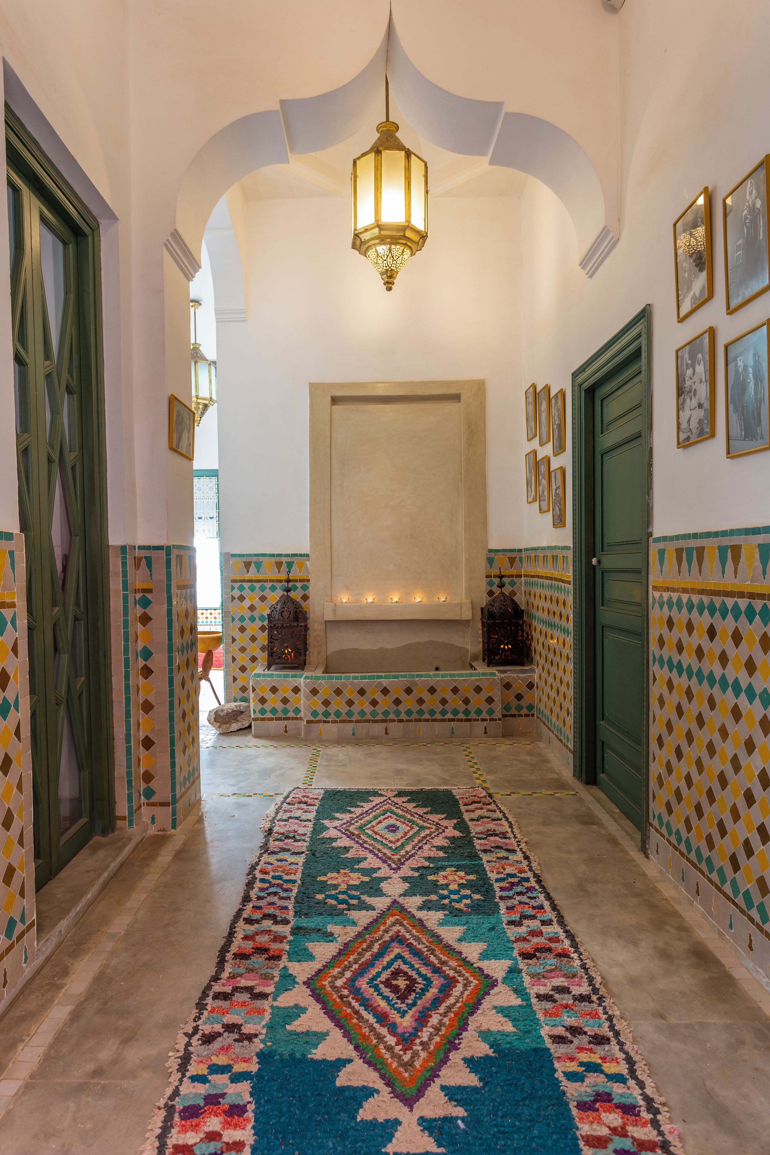 Um corredor com carpete estampado, uma porta verde e um aplique na parede.