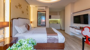 Quarto de hotel com cama, mesa de cabeceira, televisão e vista para a cozinha e varanda.