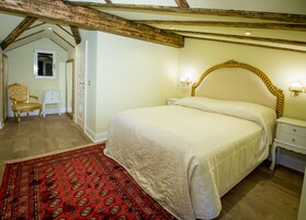 Quarto com cama grande, vigas de madeira, tapete vermelho estampado e mesa de cabeceira branca.