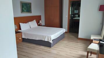 Quarto de hotel com cama, guarda-roupa de madeira, mesa de cabeceira, abajur e escrivaninha com cadeira.