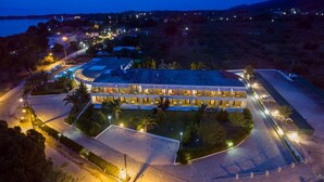 Hotel de vários andares com piscina, rodeado por palmeiras e área de estacionamento.