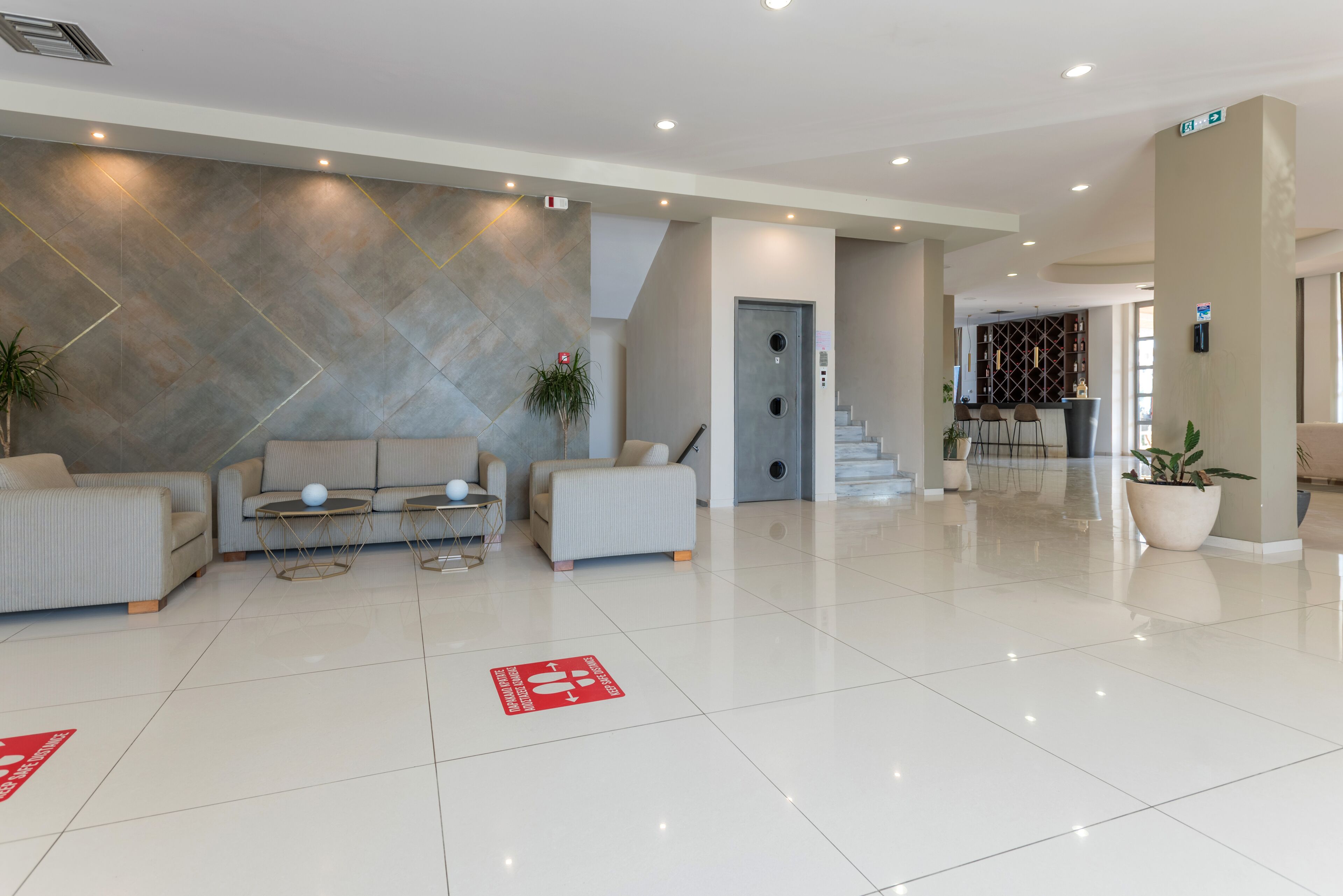 Um hall amplo com design moderno, incluindo uma área de estar com sofás e uma mesa de centro, um balcão de recepção e uma escadaria que leva aos andares superiores.
