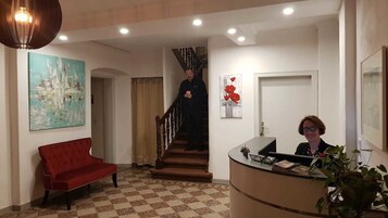 Uma área de recepção com um sofá vermelho, um balcão de atendimento, uma escada e um quadro na parede.