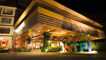 Entrada de hotel com um grande letreiro com as letras 'T' e 'F', uma decoração em formato de coração e fachada bem iluminada.