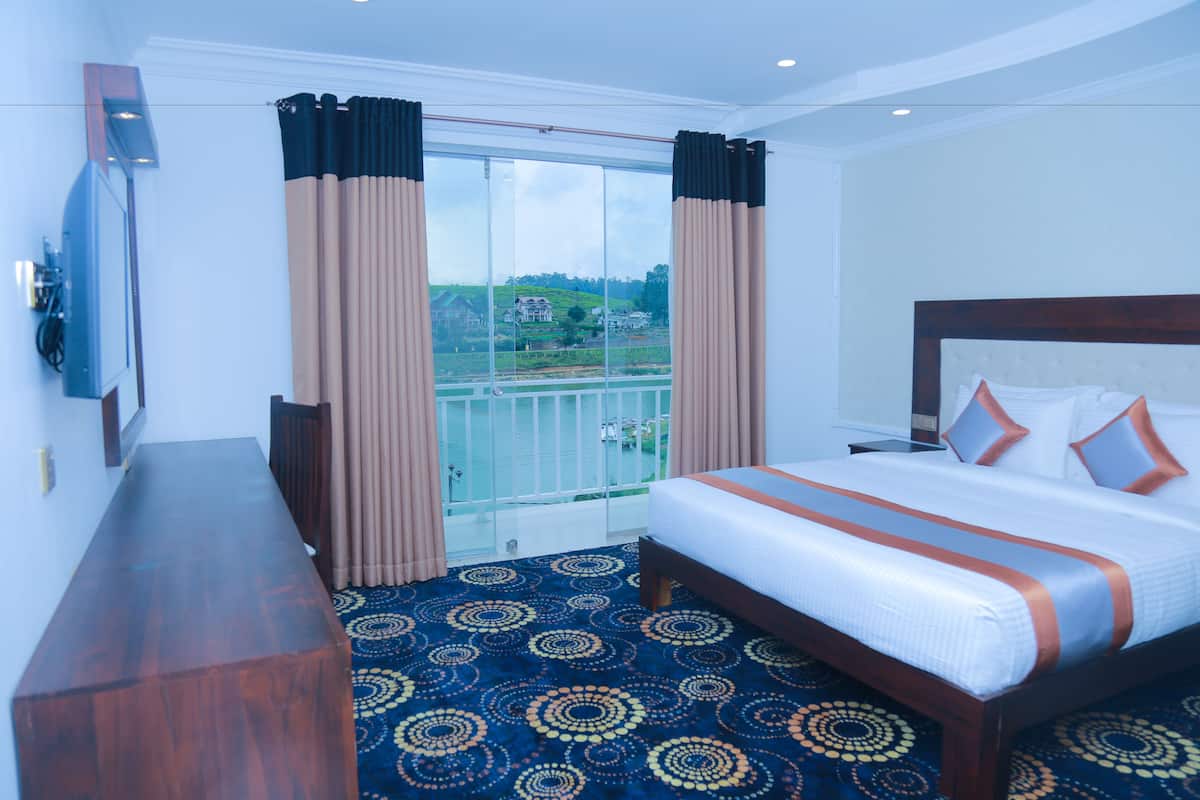 Quarto de hotel com uma cama grande, penteadeira de madeira e vista para a água e vegetação.