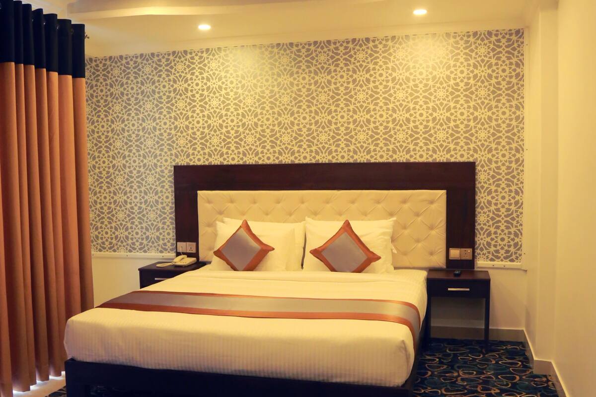 Quarto de hotel bem arrumado com uma cama grande, uma mesa de cabeceira e um tapete estampado.