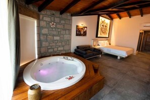 Quarto com parede de pedra, uma banheira grande, cama e sofá.