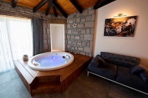Quarto com parede de pedra, um banco de madeira, uma banheira grande e um sofá de cor escura.