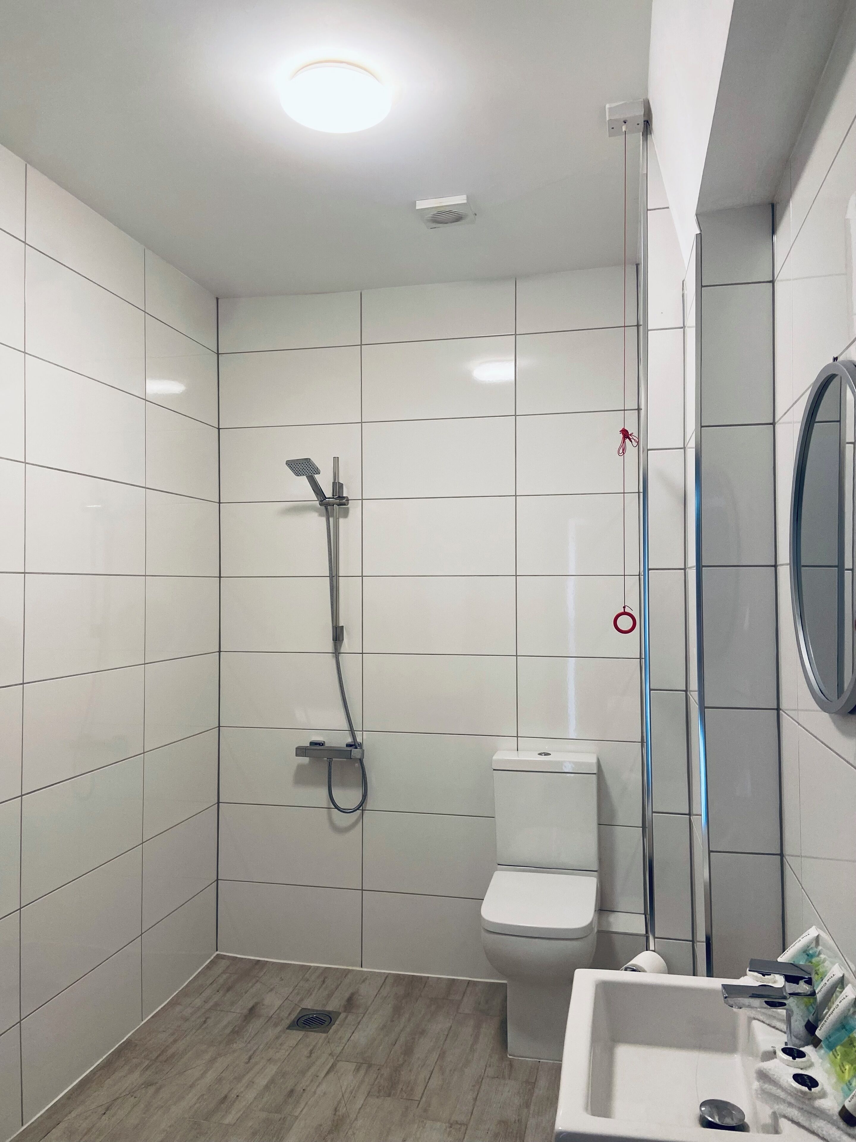 Uma casa de banho pequena e moderna com azulejos brancos, chuveiro, sanita e lavatório.