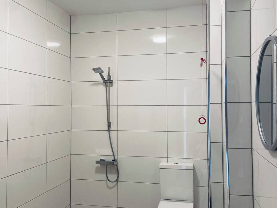 Uma casa de banho pequena e moderna com azulejos brancos, chuveiro, sanita e lavatório.