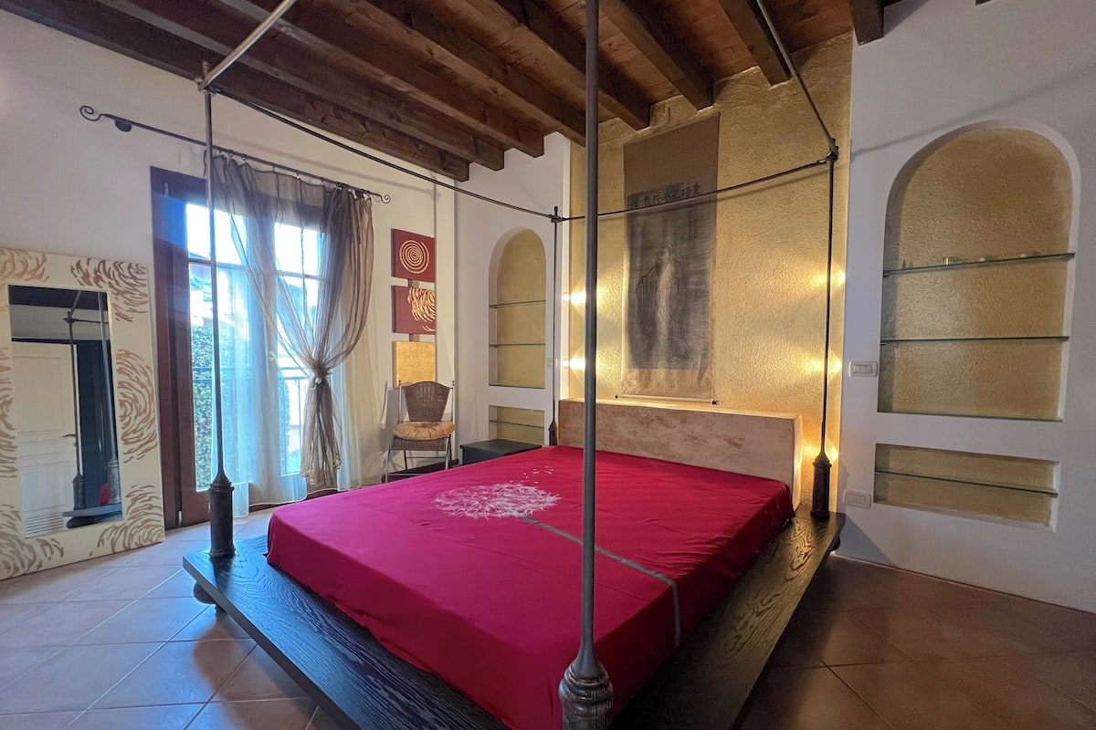 Um quarto com uma cama, uma cadeira, uma janela com cortinas e um quadro na parede.