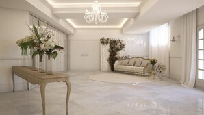 Um quarto espaçoso com piso de mármore, um sofá, uma mesa com vasos de flores e um lustre.
