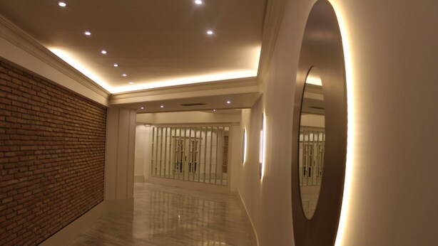 Um corredor moderno com piso polido, parede decorada com tijolos e um espelho circular grande.