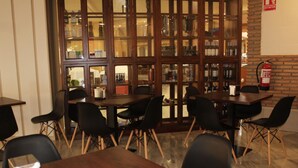 Interior de restaurante com mesas de madeira e cadeiras pretas, parede de tijolos e extintor de incêndio.