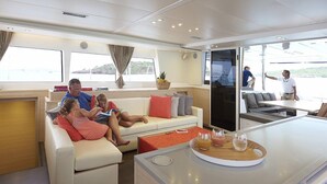 Interior de iate com sala de estar, área de jantar e vista para o mar.