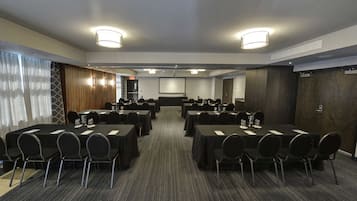 Uma sala de conferências com várias mesas e cadeiras, uma tela de projetor e piso coberto de carpete.