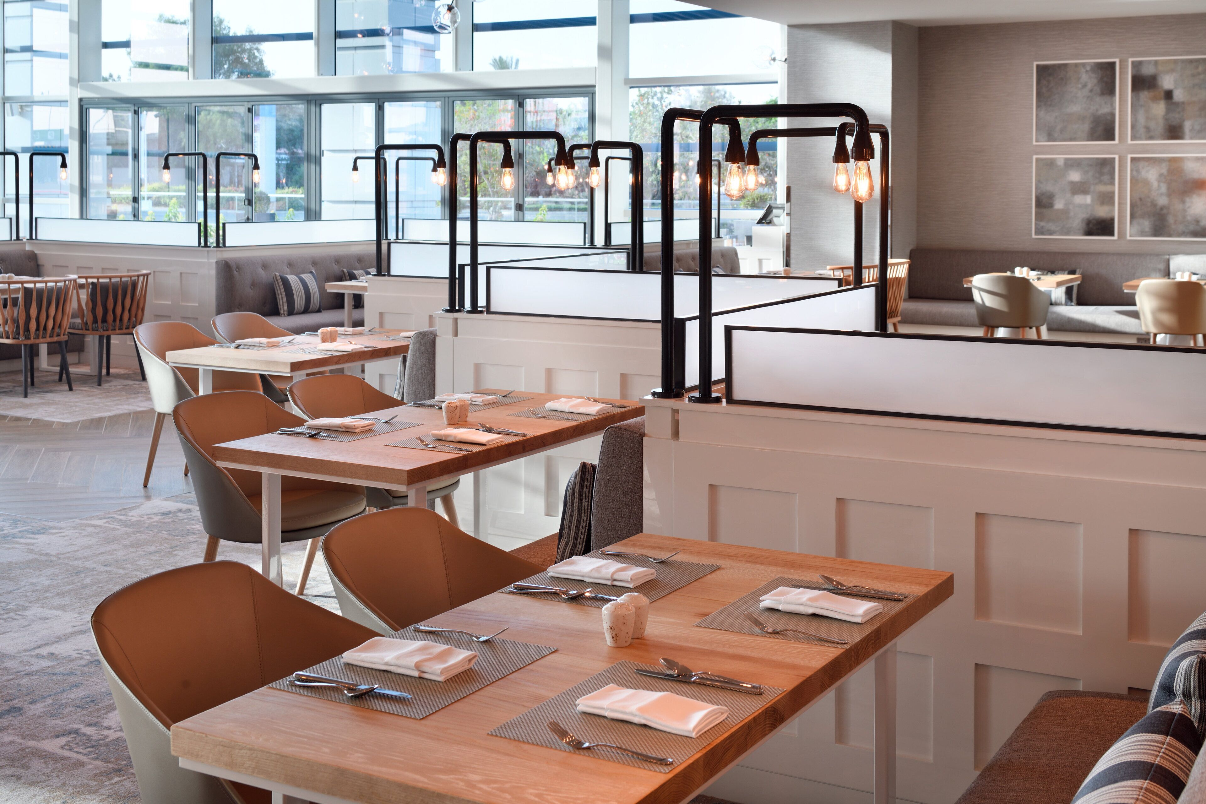 Um restaurante moderno com mesas de madeira, assentos acolchoados e iluminação pendente.