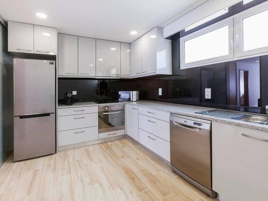 Cozinha moderna com armários brancos, eletrodomésticos de aço inoxidável e uma grande janela que oferece iluminação natural.