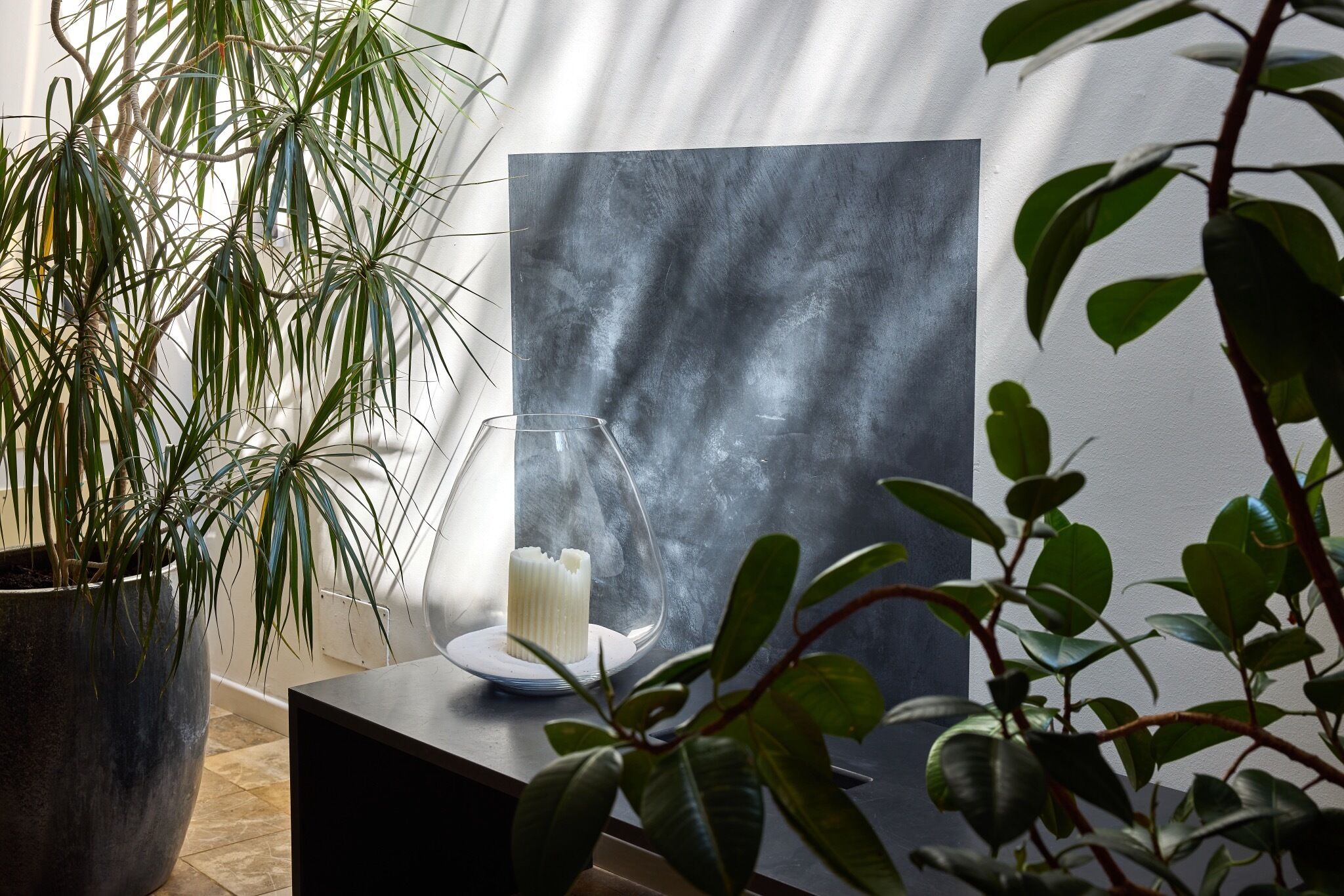 Um quarto com uma planta em vaso, um castiçal de vidro e uma obra de arte emoldurada sobre uma mesa de cabeceira de madeira escura.