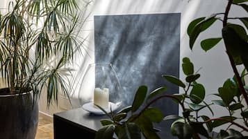 Um quarto com uma planta em vaso, um castiçal de vidro e uma obra de arte emoldurada sobre uma mesa de cabeceira de madeira escura.