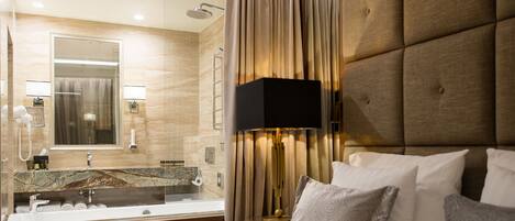 Quarto de hotel moderno com uma cama grande, um espelho, toucador com pia e uma janela ampla com cortinas.