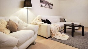 Uma sala de estar moderna com dois sofás brancos, um abajur preto, uma mesinha e um quadro na parede.