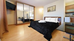 Um quarto com cama, espelho, televisão e escrivaninha com luminária.