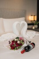 Uma cama com travesseiros em formato de coração, um buquê de flores e uma garrafa de vinho.