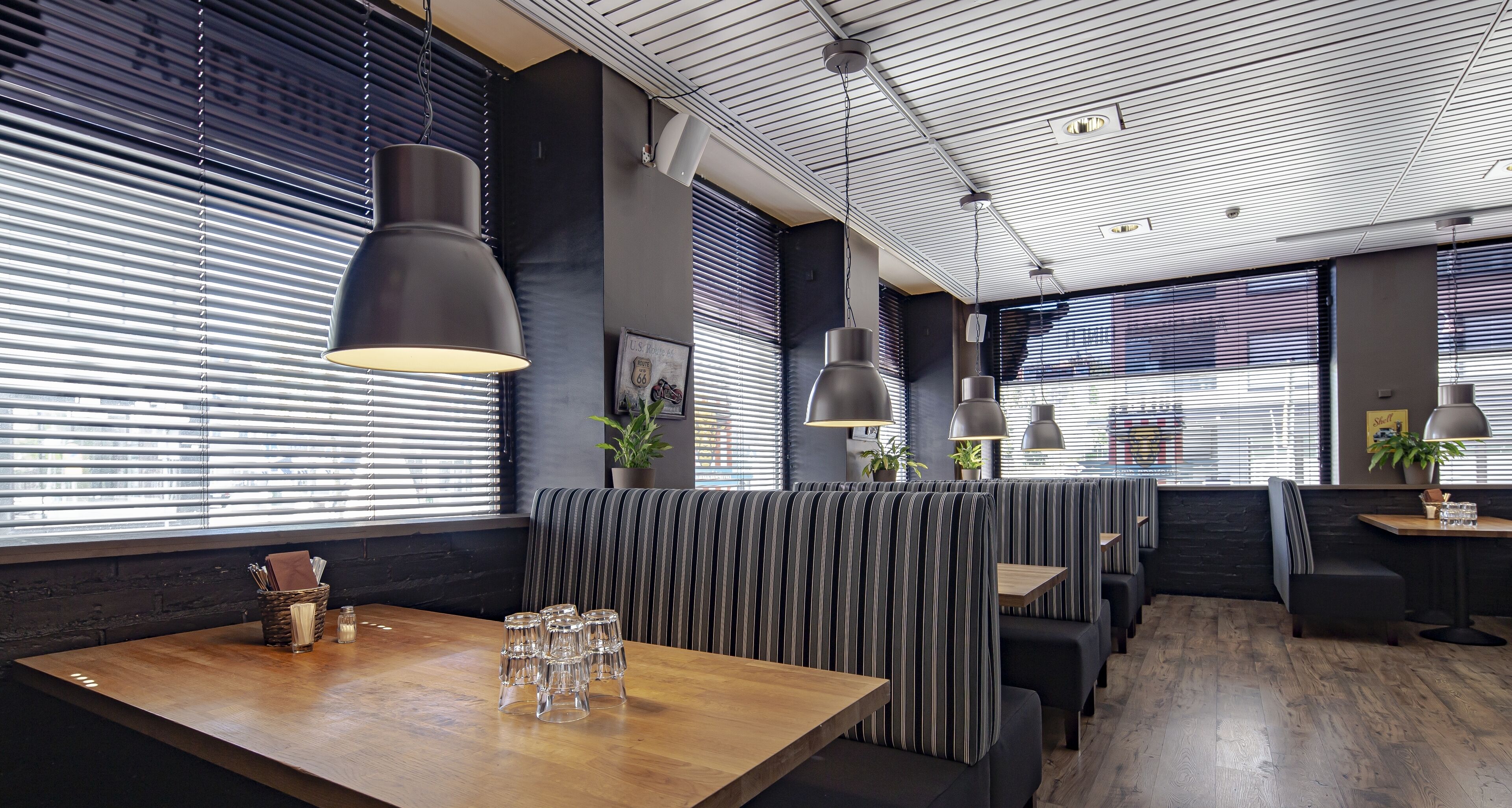 Interior de restaurante moderno com assentos estofados listrados, mesas de madeira e iluminação pendente.