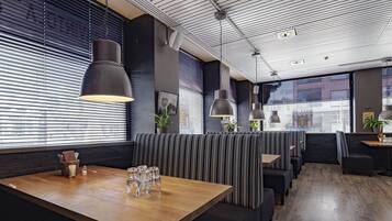 Interior de restaurante moderno com assentos estofados listrados, mesas de madeira e iluminação pendente.