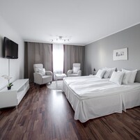 Quarto de hotel moderno com uma cama grande, duas poltronas, uma mesinha, televisão e um quadro na parede.