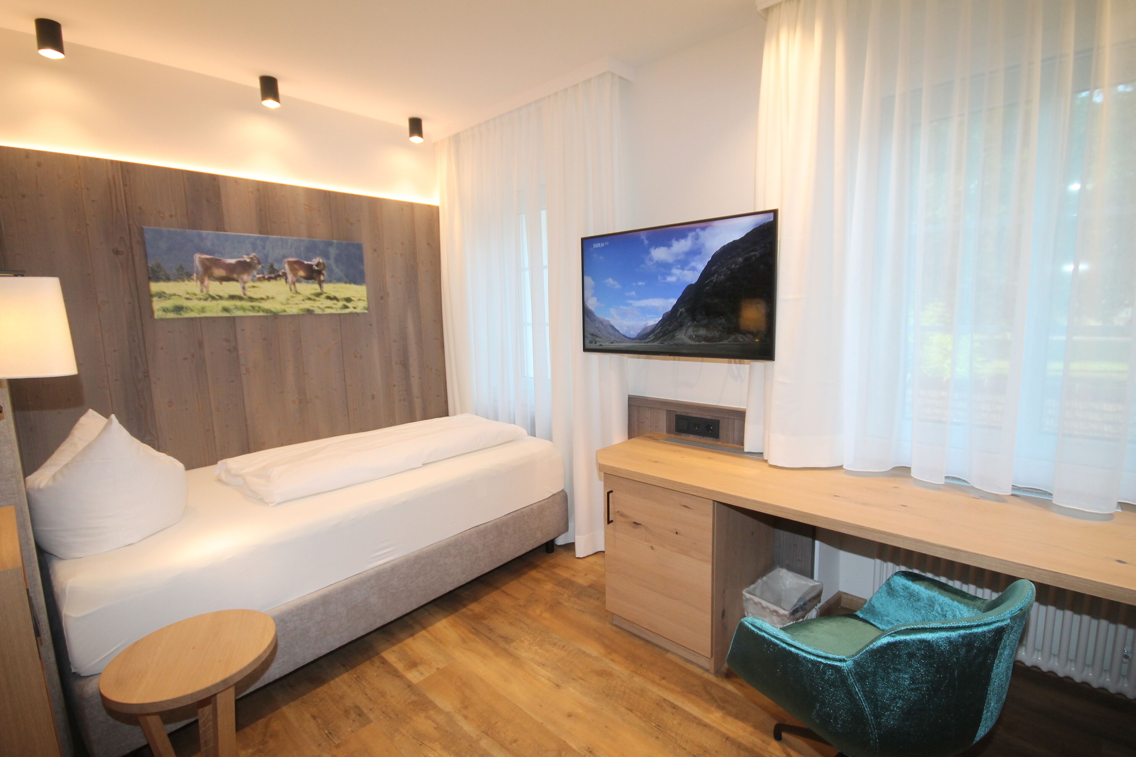 Quarto de hotel moderno com uma cama, uma escrivaninha, uma cadeira, uma televisão e um quadro na parede.