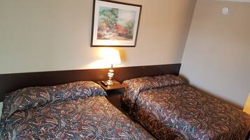 Quarto de hotel com duas camas, uma mesa de cabeceira com abajur e um quadro na parede.