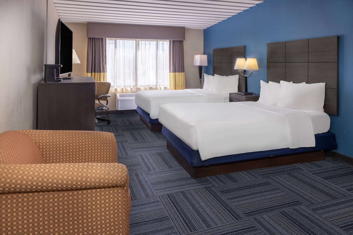 Quarto de hotel com duas camas, uma escrivaninha, uma televisão e uma cadeira.