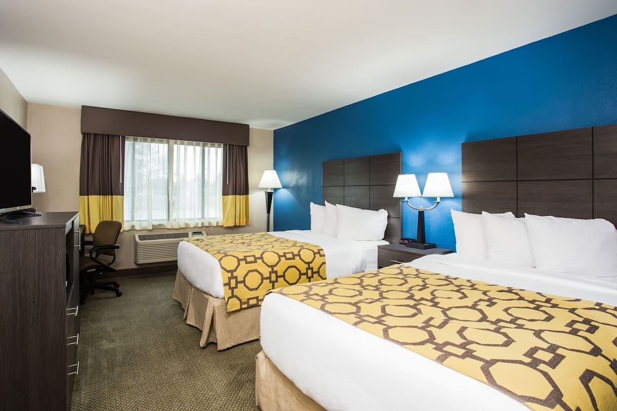 Quarto de hotel com duas camas, uma escrivaninha, televisão e janela com cortinas.
