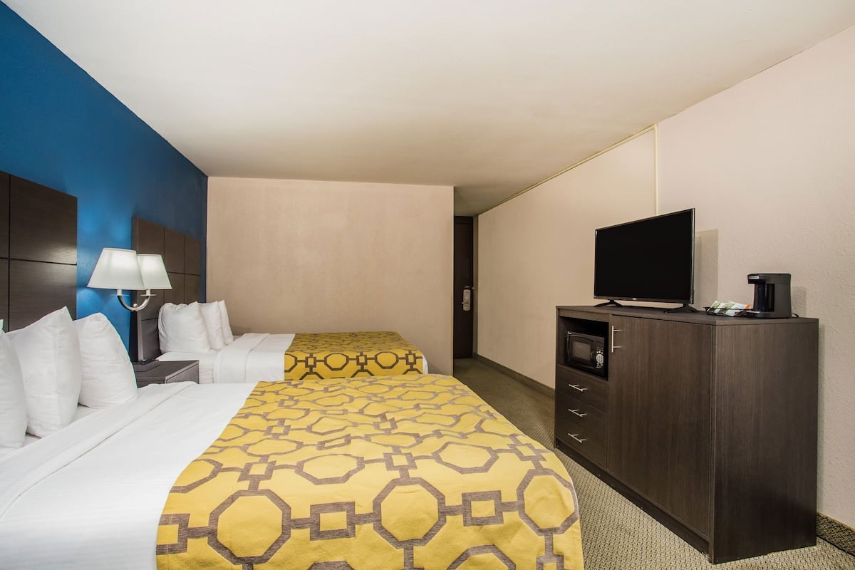 Quarto de hotel com cama, televisão, escrivaninha com candeeiro e cómoda.