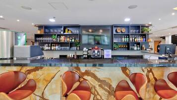 Uma área de bar moderna com uma TV de tela plana, prateleiras com garrafas de bebidas e cadeiras vermelhas.
