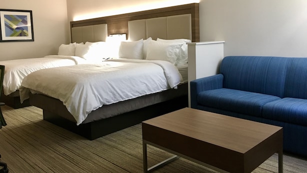 Quarto de hotel com duas camas, um sofá azul e uma mesa de centro de madeira.
