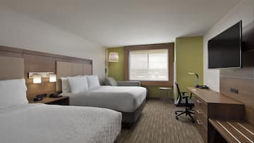 Quarto de hotel com duas camas, uma mesa, uma cadeira, uma televisão e uma janela.