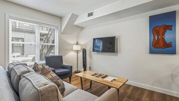 Uma sala de estar moderna com sofá, poltrona, luminária de chão e uma mesa com controles remotos.