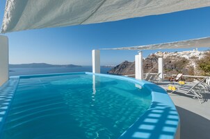 Uma piscina azul cristalina com vista para o mar e paisagem rochosa ao fundo.